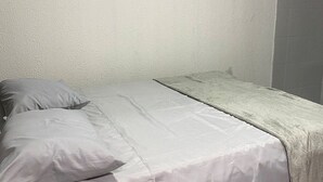 Uma cama de solteiro com colchão e almofadas brancas, cobertor cinza e cabeceira cinza.