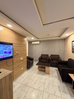 Uma sala de estar moderna com televisão de tela plana, sofás escuros, um armário de madeira e parede listrada.