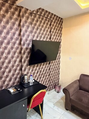Quarto com parede acolchoada, TV de tela plana, escrivaninha com cadeira, sofá e garrafa de água na escrivaninha.