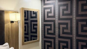 Quarto de hotel com cama, guarda-roupa de madeira, espelho e parede com padrão geométrico.