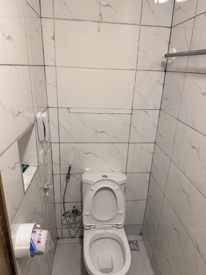 Um banheiro pequeno com azulejos, vaso sanitário, secador de mãos e dispensador de toalhas de papel.