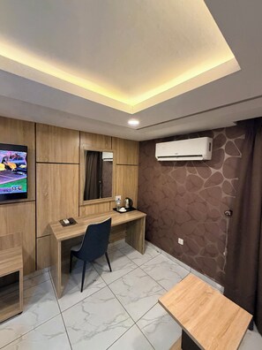 Quarto de hotel com escrivaninha de madeira, cadeira, televisão, aparelho de ar condicionado e parede estampada.