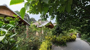 Um caminho leva a um edifício de madeira rodeado por vegetação exuberante e plantas floridas.