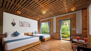Quarto com duas camas, piso de madeira, área de refeições com mesa e cadeiras, e vista através de uma porta de vidro.