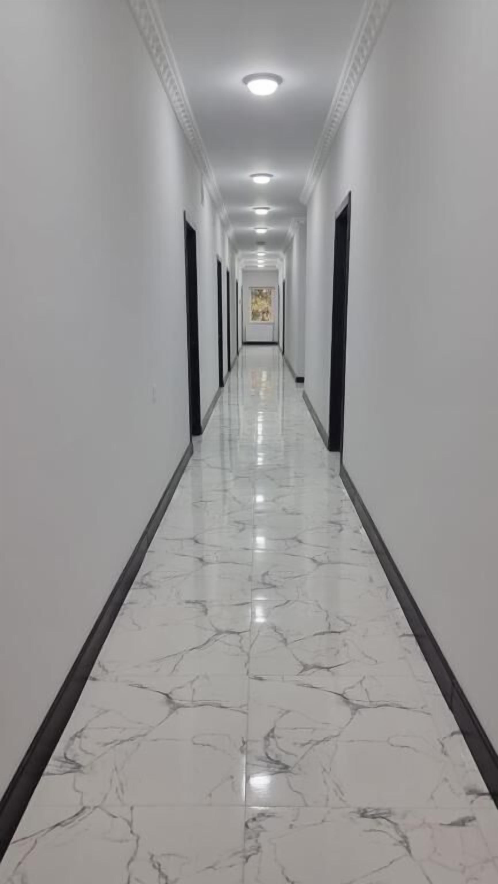 Um corredor comprido e estreito, com paredes brancas e chão de mármore.