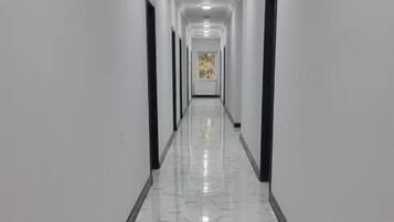 Um corredor comprido e estreito, com paredes brancas e chão de mármore.