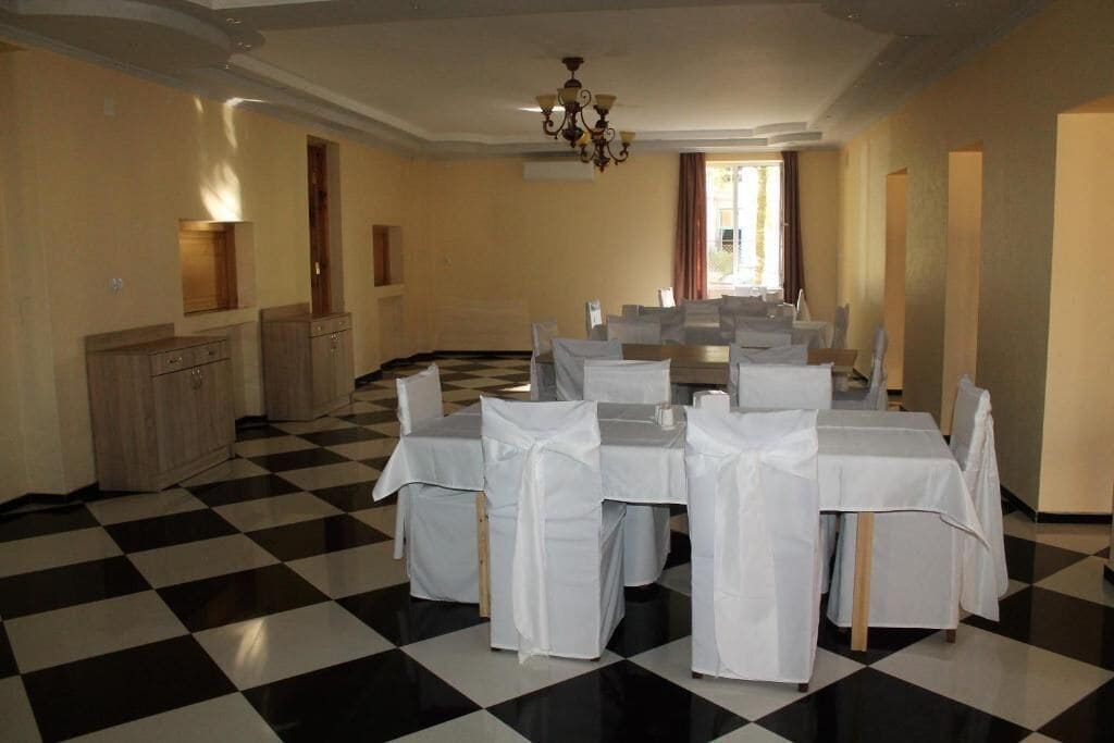 Um espaço de refeições de hotel com chão xadrez, mesas com toalhas brancas e cadeiras.
