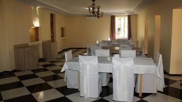 Um espaço de refeições de hotel com chão xadrez, mesas com toalhas brancas e cadeiras.
