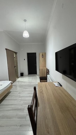 Quarto com mesa de jantar de madeira, televisão fixada na parede e luminária pendente.