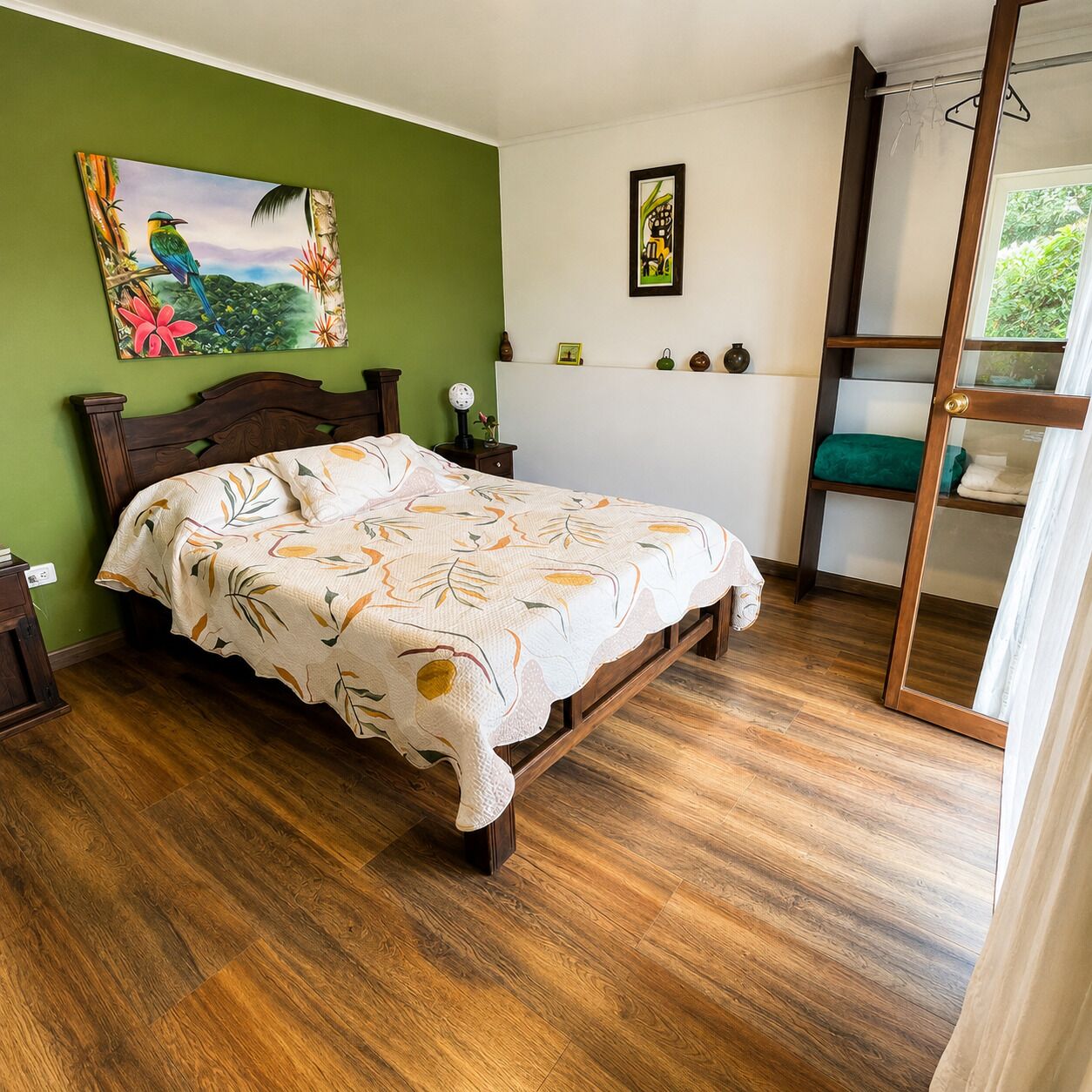 Quarto com cama de madeira, paredes verdes, um quadro e um espelho.