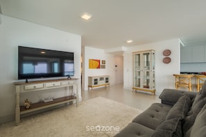 Uma sala de estar moderna com uma televisão de tela plana, um sofá cinza, um console branco e um armário de vidro.