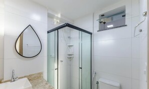 Casa de banho moderna com chuveiro de vidro, espelho redondo e lavatório branco.