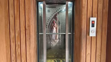 Um elevador com visor digital mostrando o número 4, painéis de madeira nas paredes e piso estampado.
