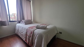 Uma cama de solteiro com edredom branco e vermelho estampado, um travesseiro e um cobertor.