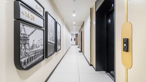 Corredor com fotografias a preto e branco emolduradas nas paredes, elevador moderno com detalhes dourados e chão revestido de azulejos.