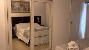 Quarto com cama, guarda-roupa com espelho e mesa de cabeceira com abajur.