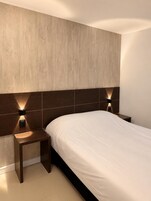 Quarto de hotel com cama grande, duas mesas de cabeceira e iluminação embutida na parede.