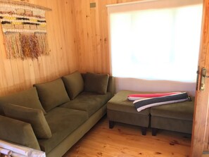 Um quarto aconchegante com um sofá verde, um pequeno banquinho e um painel de parede tecido.