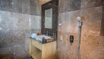 Casa de banho com lavatório com divisória de vidro, um espelho grande e chuveiro com duche manual.