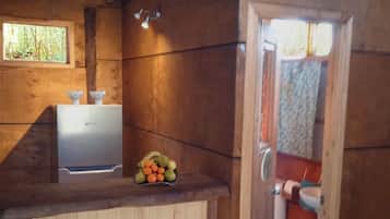 Interior de cabana de madeira, com bancada de cozinha, janela pequena e porta que dá para um banheiro.