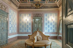 Quarto com uma cadeira decorativa, paredes estampadas e porta verde.