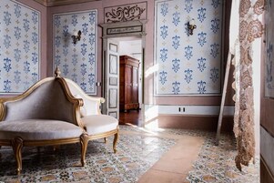 Quarto com uma poltrona clássica, papel de parede estampado e um armário de madeira.