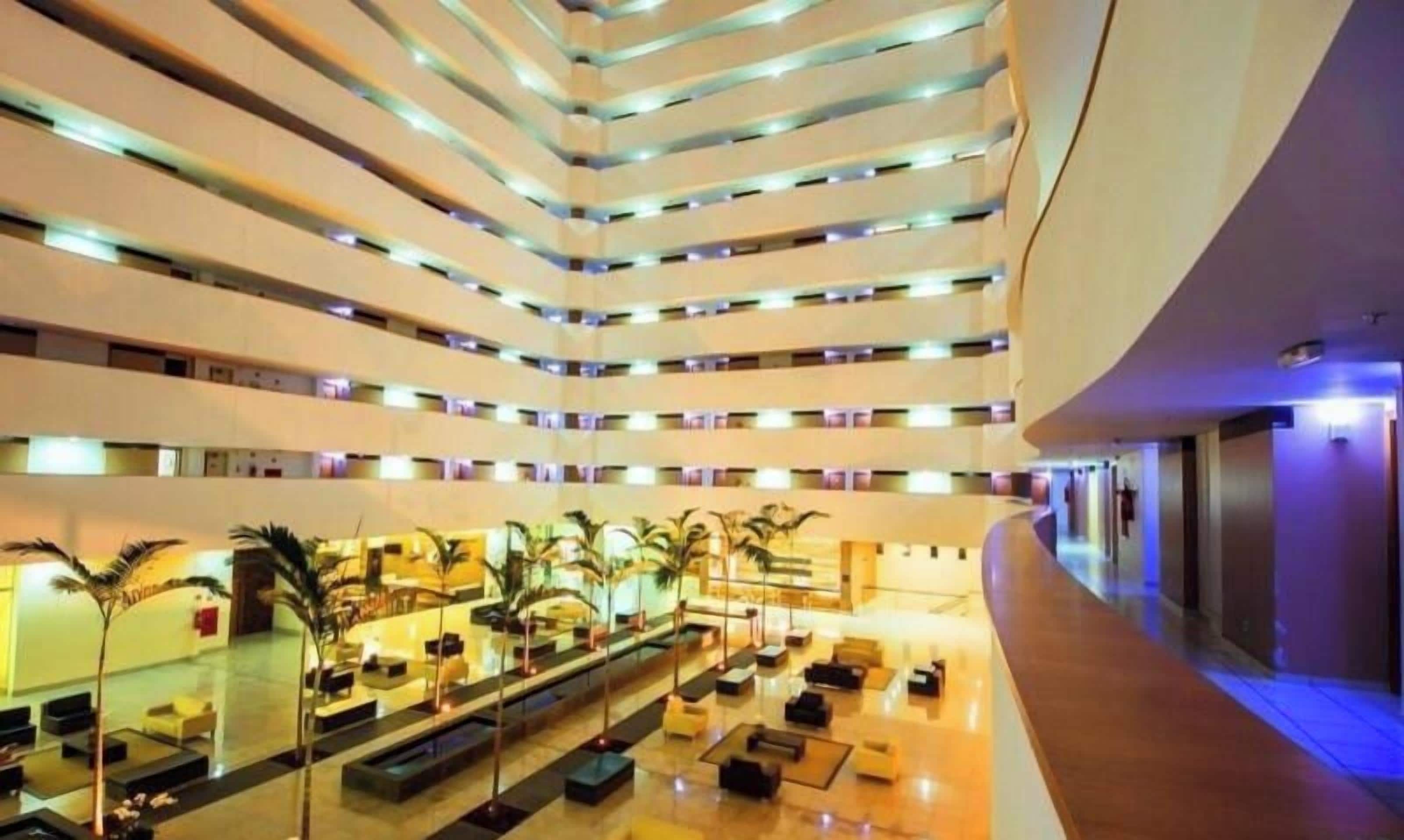 Um saguão de hotel com vários níveis, um átrio central, áreas de estar e uma passarela curva.