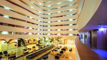 Um saguão de hotel com vários níveis, um átrio central, áreas de estar e uma passarela curva.