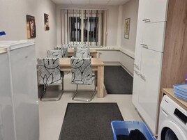 Quarto pequeno e limpo com mesa, cadeiras, máquina de lavar e frigorífico.