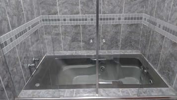 Casa de banho com banheira de hidromassagem com vedação de vidro, paredes em azulejo e área de duche.