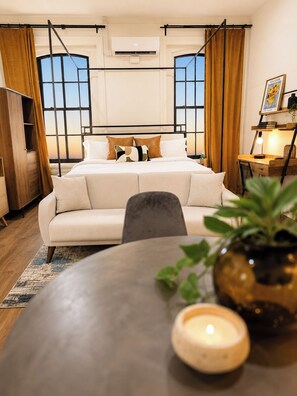 Quarto com cama, sofá, escrivaninha, cadeira, mesa, planta e vela.