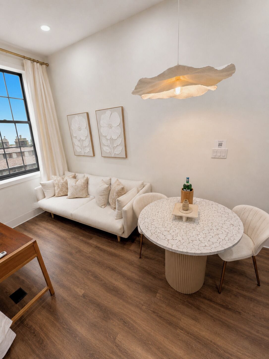 Uma sala de estar moderna com um sofá branco, uma mesa redonda e uma luminária pendente diferenciada.