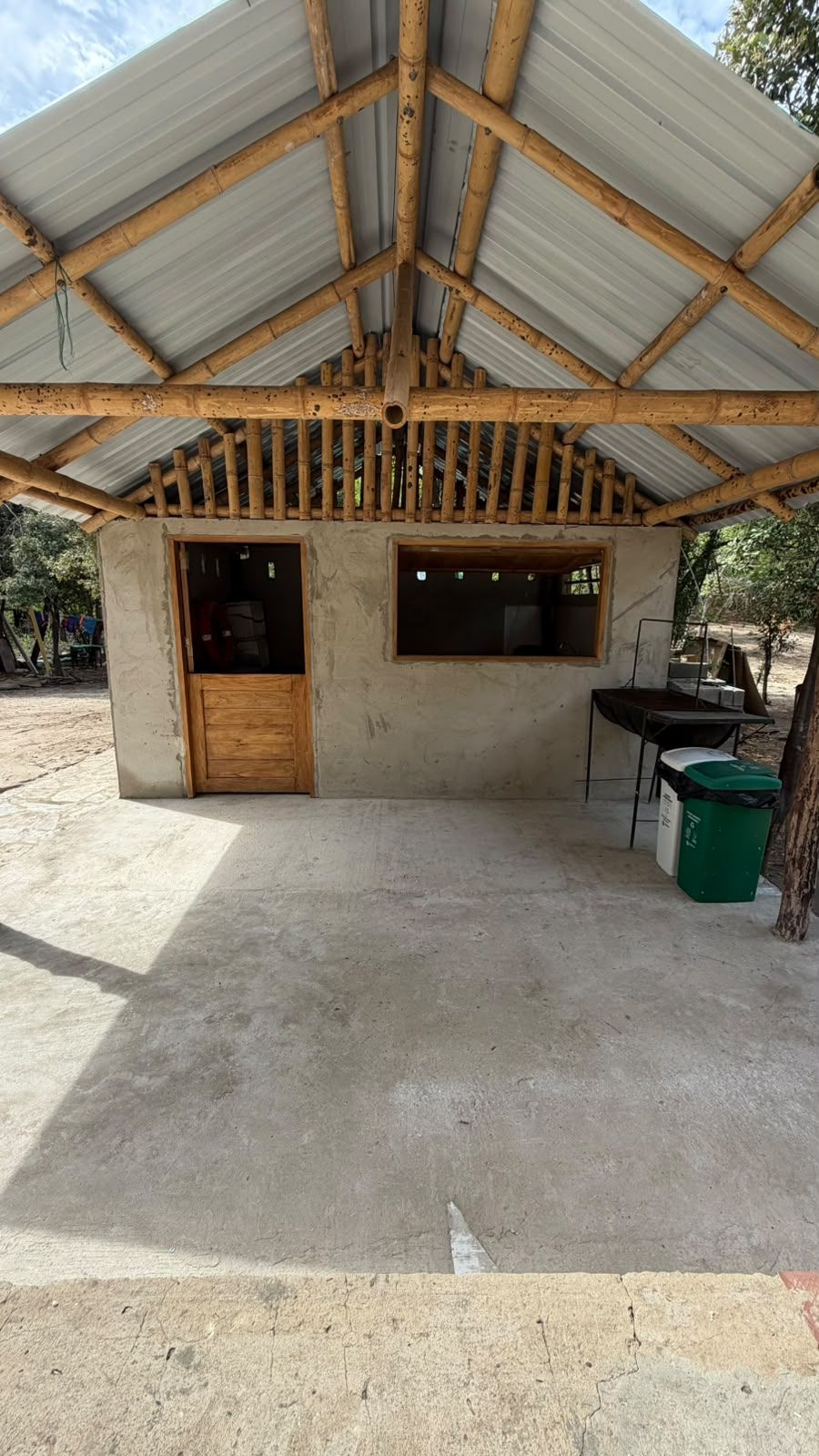Uma área externa coberta com piso de concreto, uma porta de madeira e uma janela.
