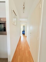 Um corredor com piso de madeira, uma porta à direita e um objeto azul ao fundo.