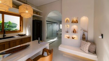Cozinha moderna com área de jantar, um sofá branco com almofadas e prateleiras na parede com objetos decorativos.