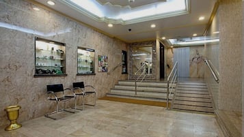 Um hall de entrada com paredes de mármore, um balcão de recepção e uma escadaria para outro andar.