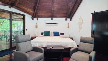 Quarto com teto de madeira, cama com almofadas, duas poltronas e uma janela grande.