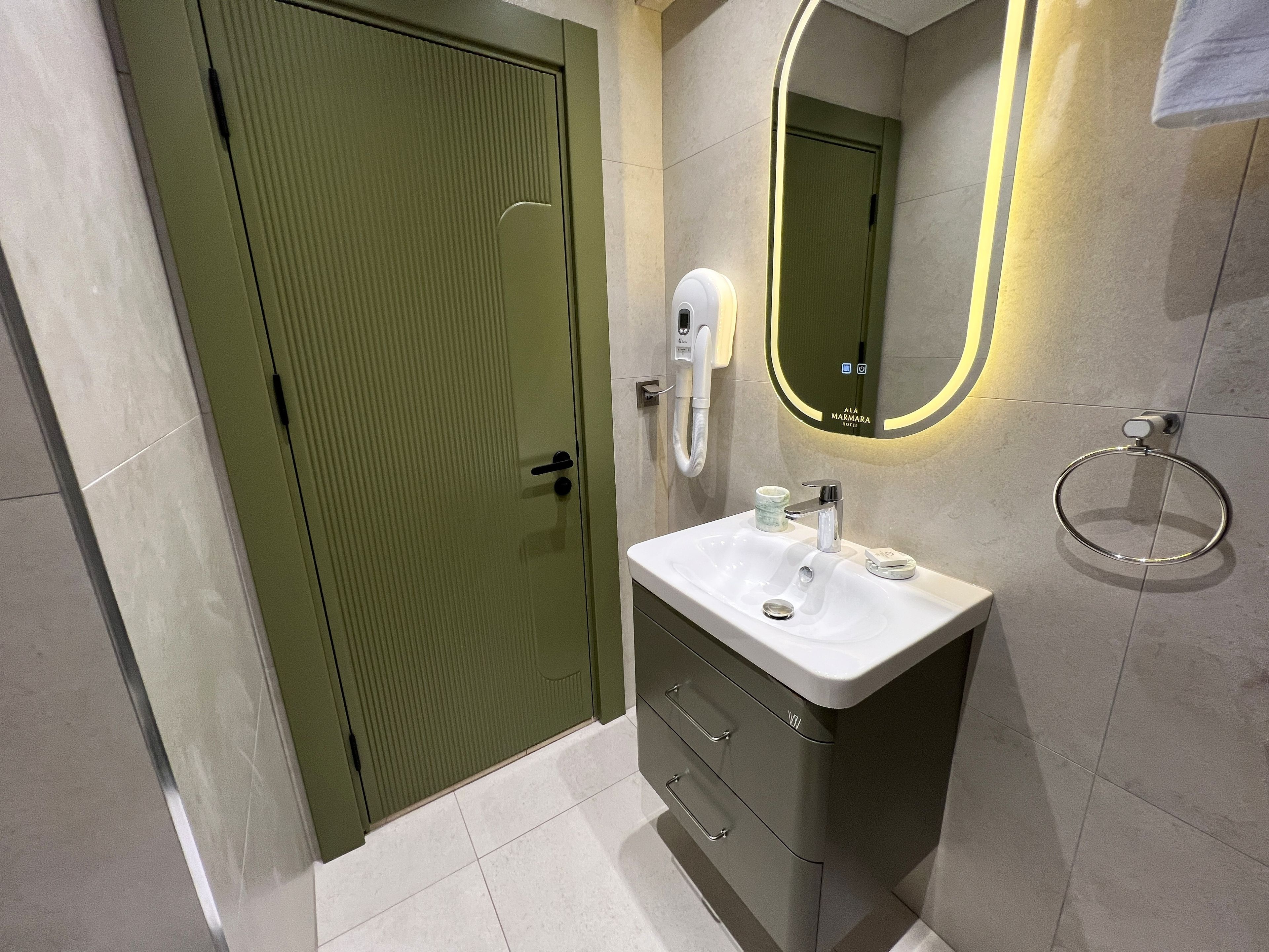 Casa de banho com porta verde, pia branca, espelho iluminado e suporte para toalhas.