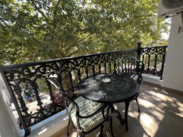 Varanda com mesa e cadeiras de metal, cercada por um guarda-corpo decorativo de metal.