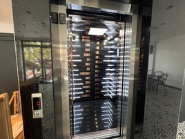 Um elevador com painel digital, interior metálico e piso estampado.