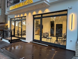 Exterior do Hotel Alamarra com grandes janelas de vidro, um deck de madeira e guarda-corrimão preto.
