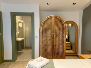 Quarto de hotel com uma cama, um guarda-roupa com espelho e um banheiro visível através de uma porta aberta.
