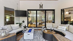 Uma sala de estar moderna com uma televisão grande, assentos confortáveis e uma porta de vidro que dá para um pátio.
