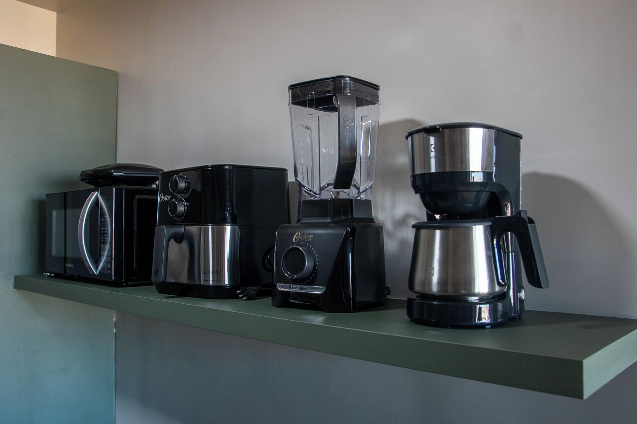 Uma bancada de cozinha com cafeteira, liquidificador e micro-ondas.