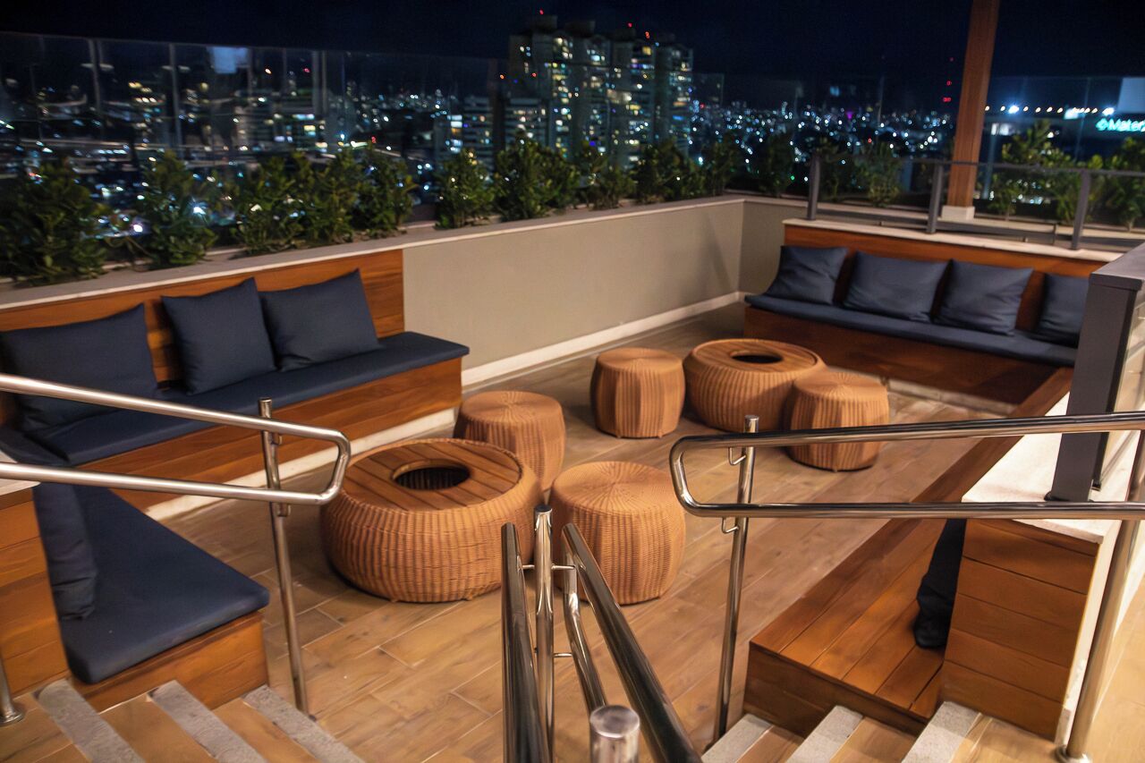 Um lounge no terraço com assentos e vista para a paisagem urbana à noite.