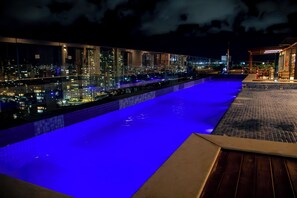 Piscina no terraço com vista para a cidade, área de estar coberta e barreira de vidro.