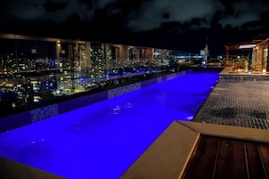 Piscina no terraço com vista para a cidade, área de estar coberta e barreira de vidro.