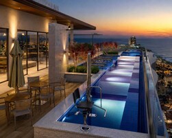 Piscina no terraço com vista para a cidade ao pôr do sol.