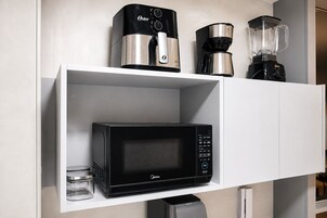 Uma prateleira na cozinha com uma cafeteira Oster preta, um jarro de café Oster preto, um liquidificador Oster preto e um micro-ondas Oster preto.