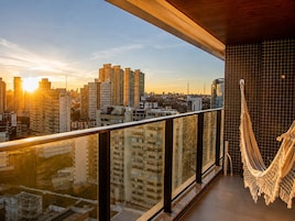 Varanda com vista para a cidade ao pôr do sol, uma rede e um muro de azulejos.